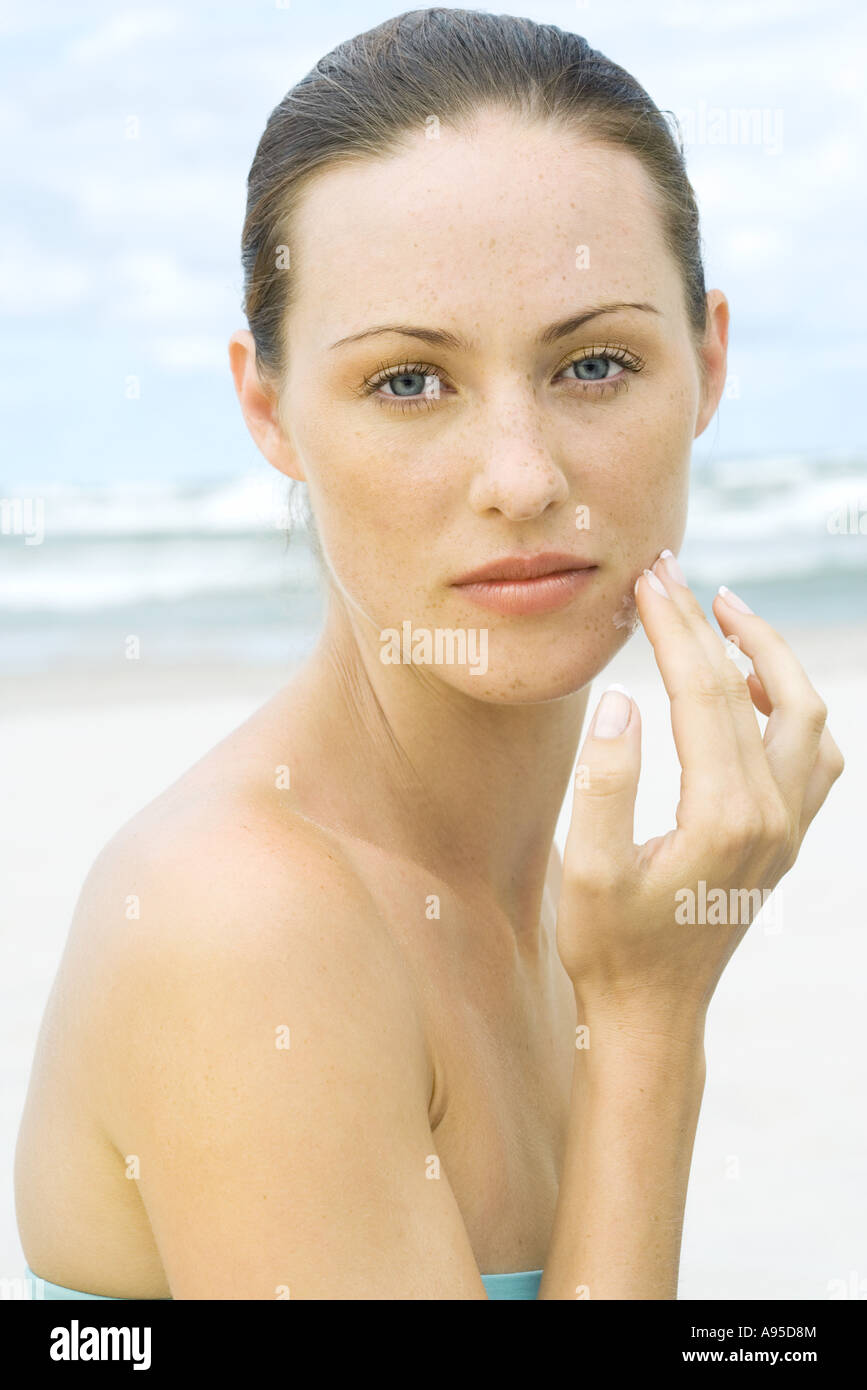 Woman applying sunscreen to face at beach, head and shoulders, portrait ...