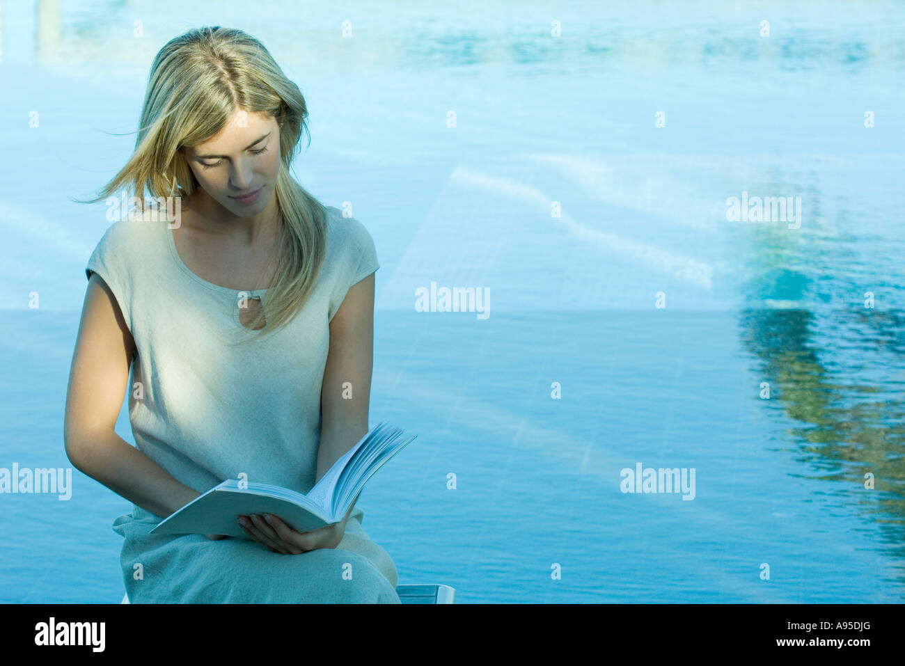 Young woman sitting by water, reading Stock Photo - Alamy
