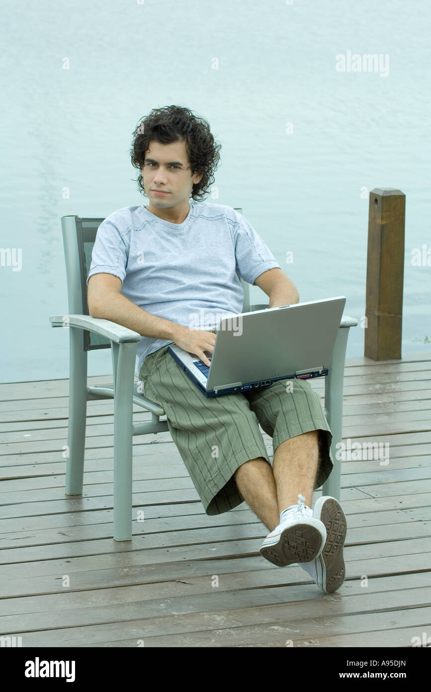 Young man sitting on dock using laptop, full length Stock Photo - Alamy