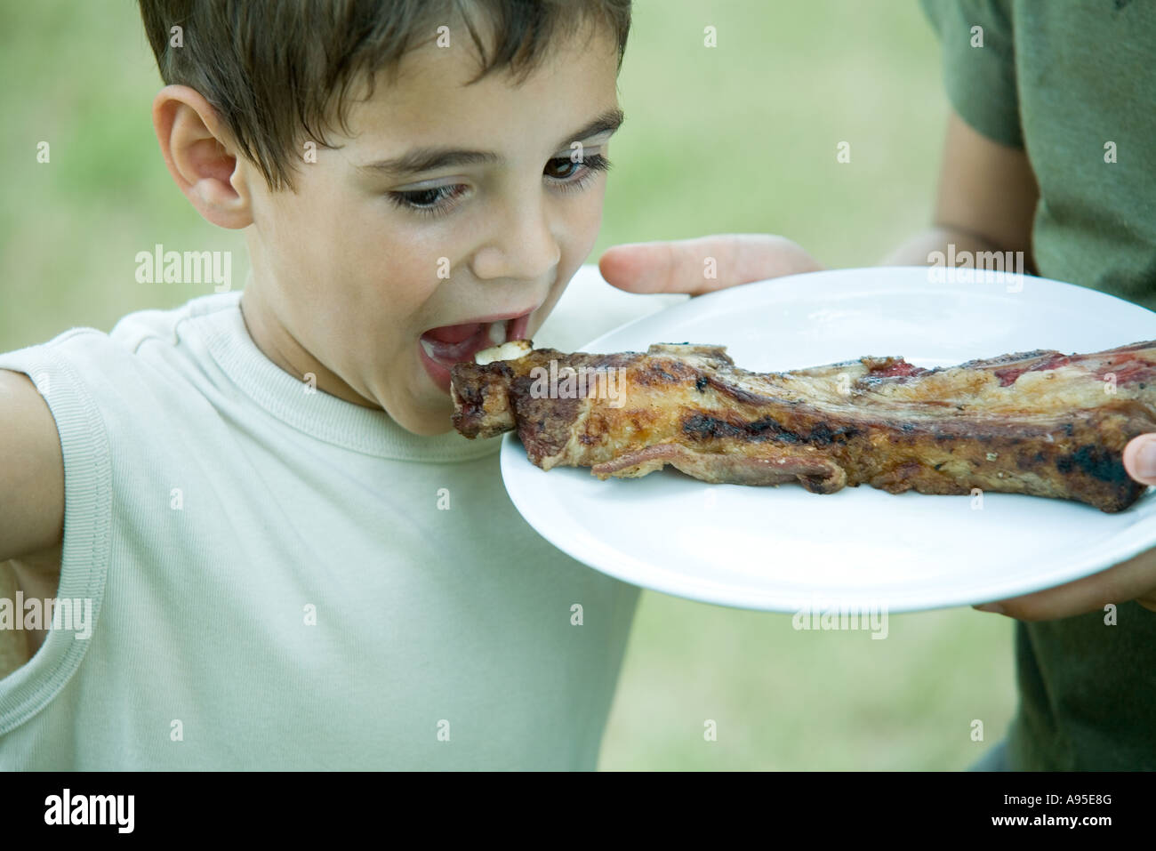 Boy eating grilled meat from plate Stock Photo - Alamy