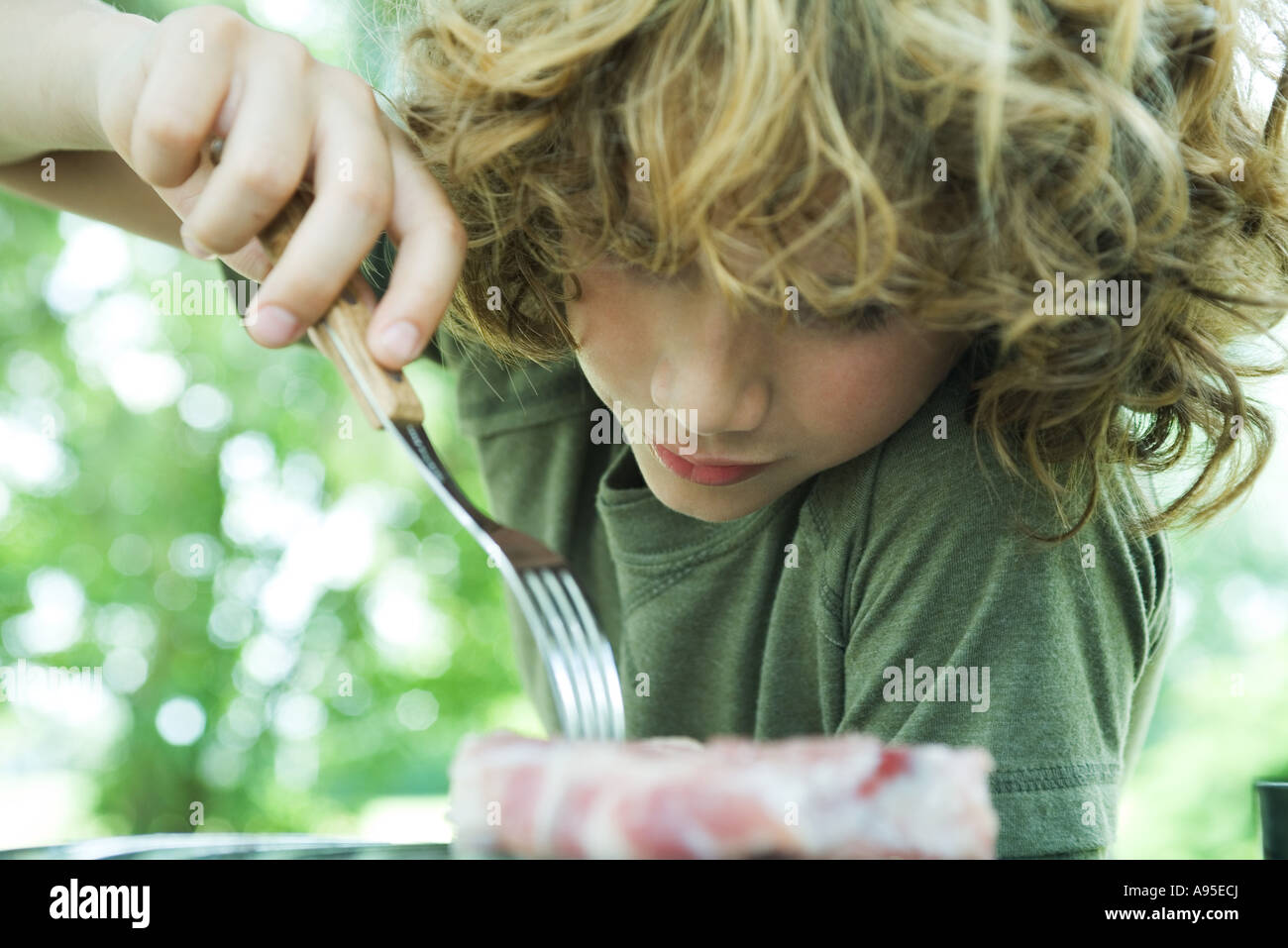 Boy picking up piece of raw meat with fork Stock Photo - Alamy
