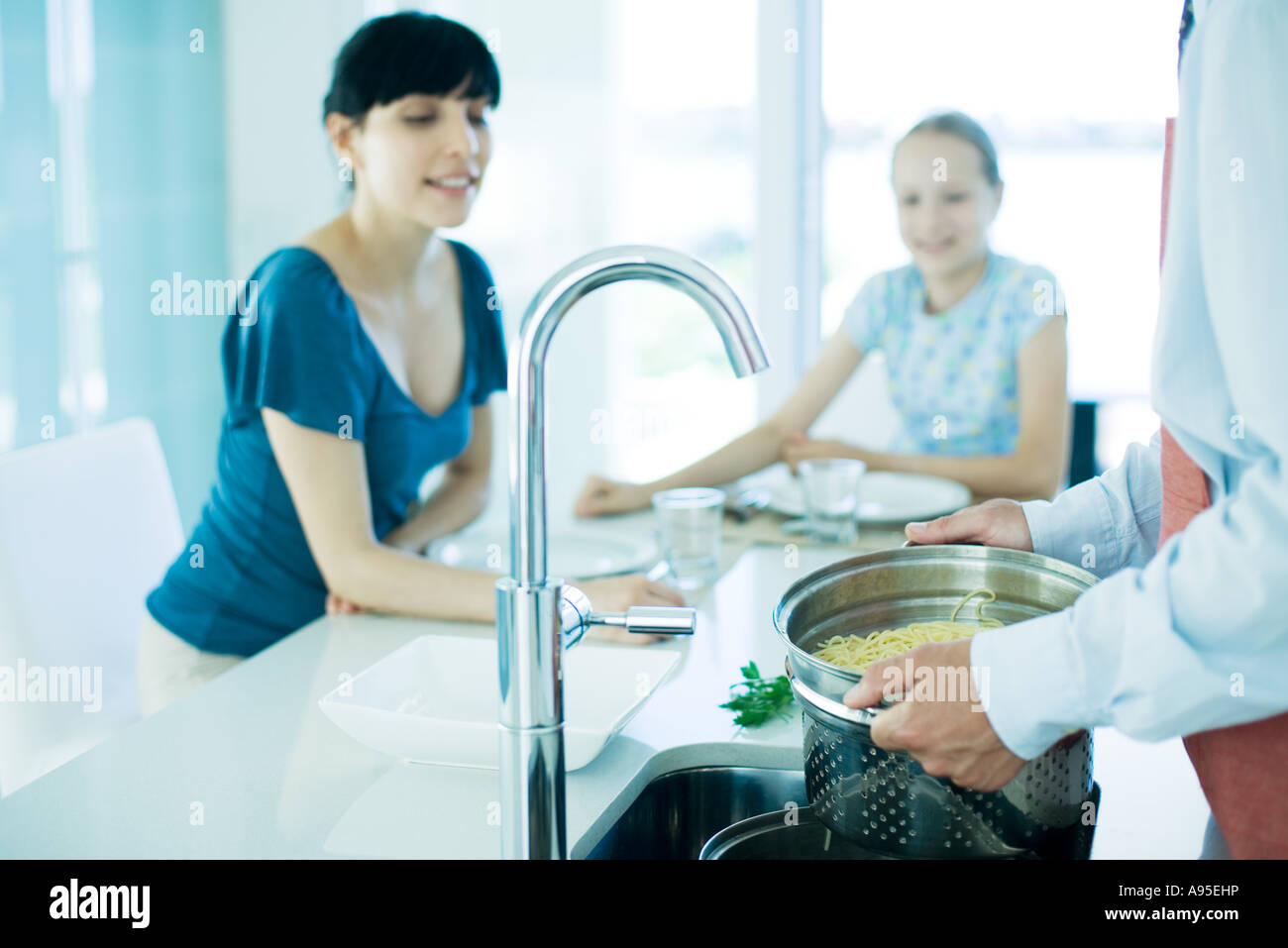 Man draining pasta while woman and girl watch Stock Photo - Alamy