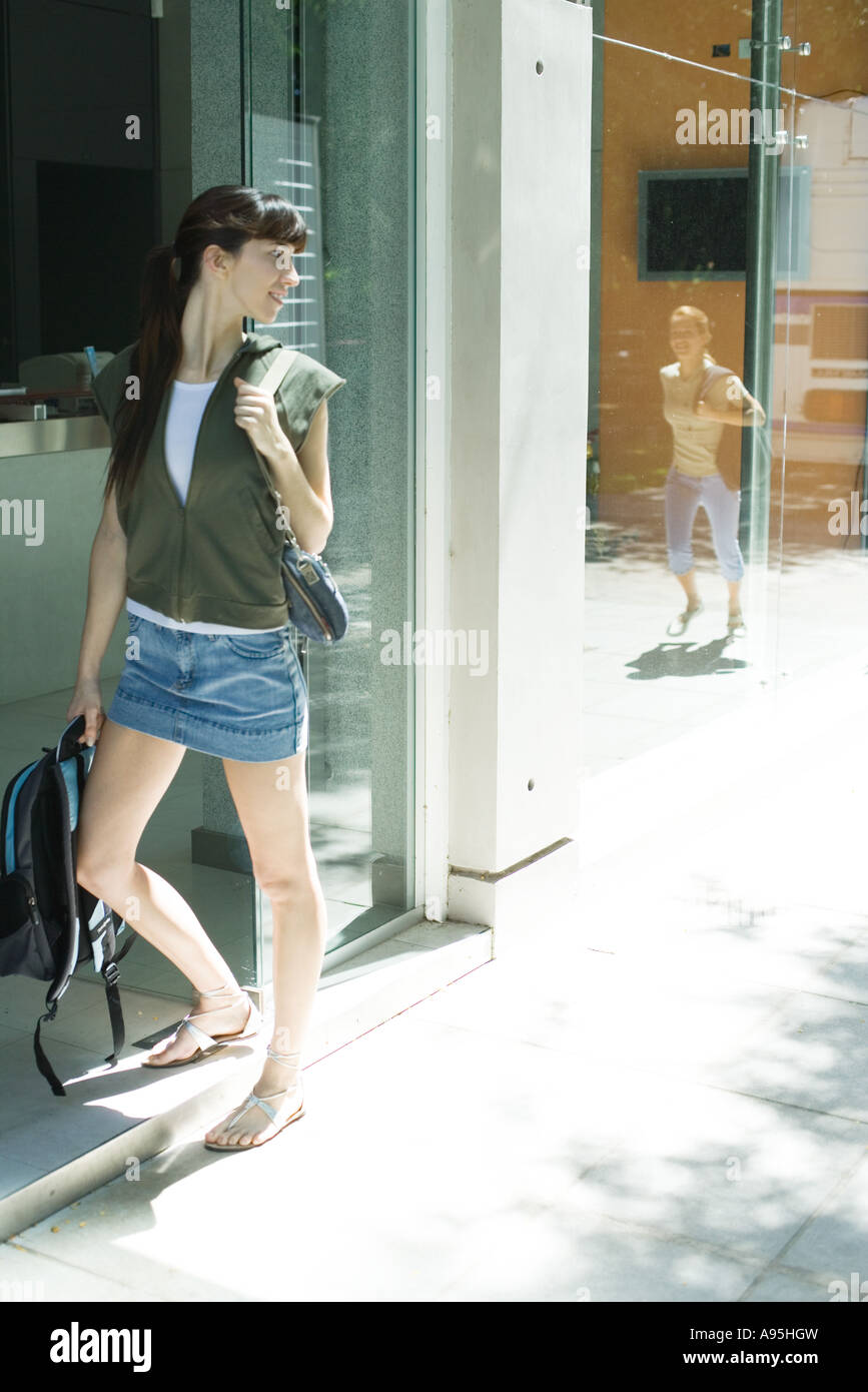 Young woman standing by entrance, looking over shoulder at friend ...