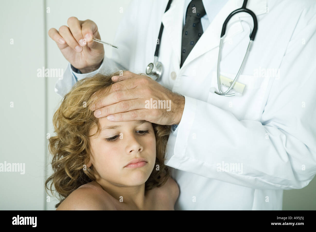 Doctor feeling boy's forehead and holding thermometer Stock Photo - Alamy