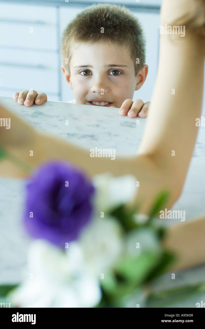 Boy looking over edge of counter, woman and flowers in blurred ...