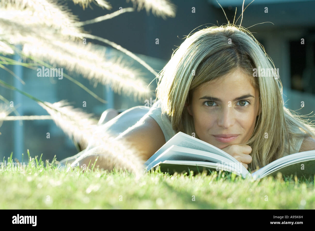 Woman lying in grass, reading book, smiling at camera Stock Photo - Alamy