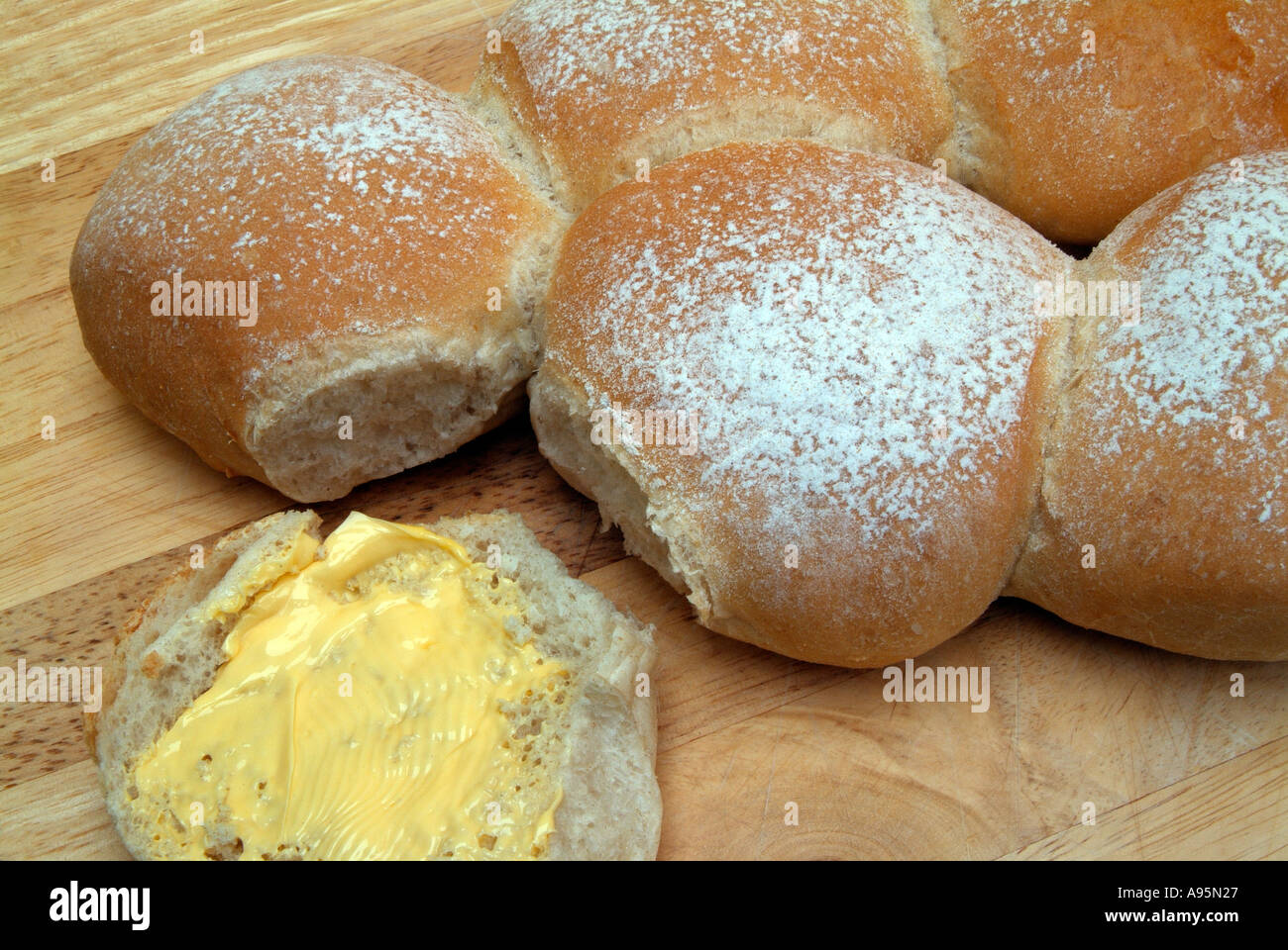 Brown floured bread rolls open with butter on breadboard Stock Photo ...