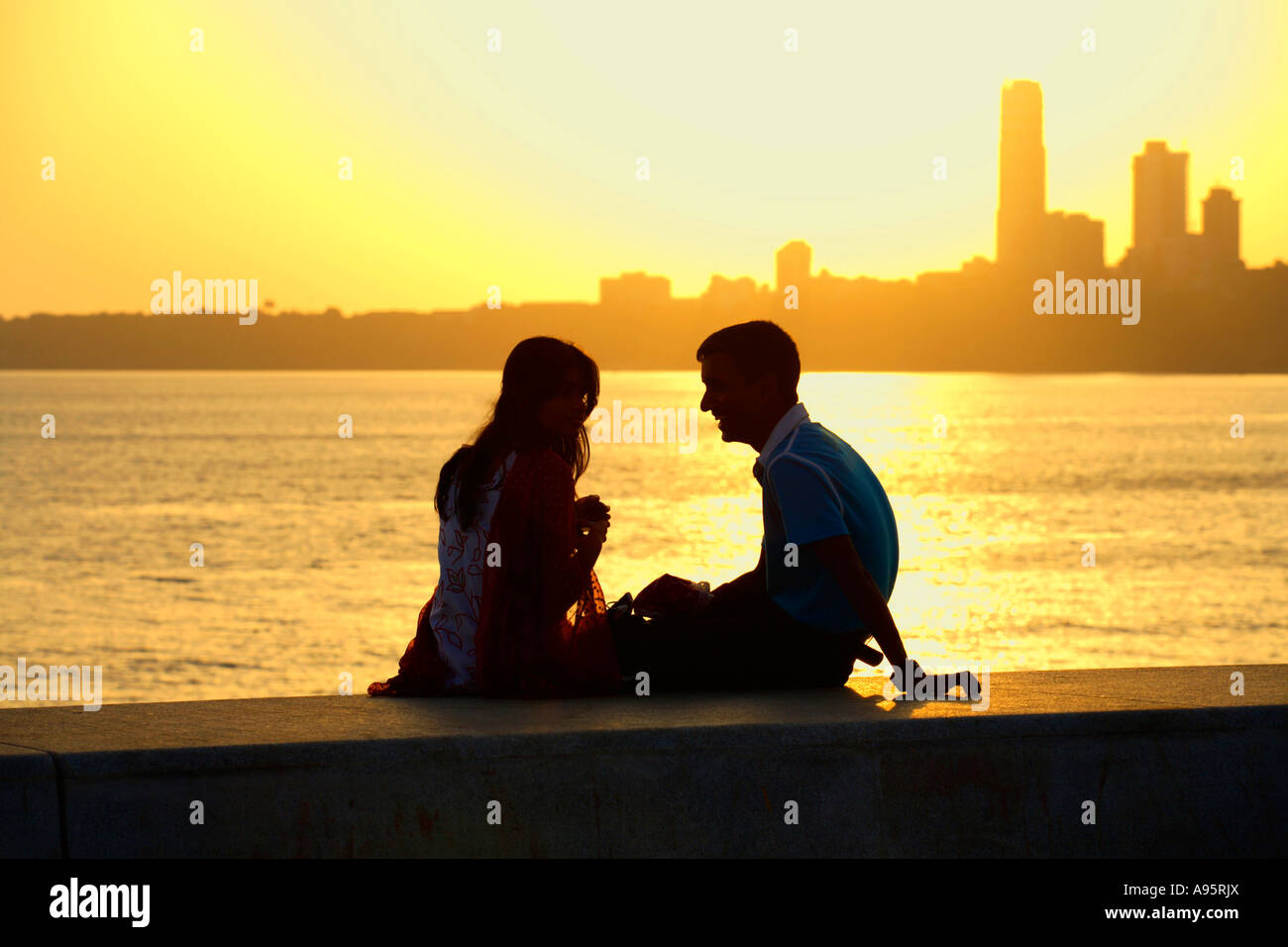 Romantic Indian couple seated on wall at sunset on Marine Drive, Mumbai ...