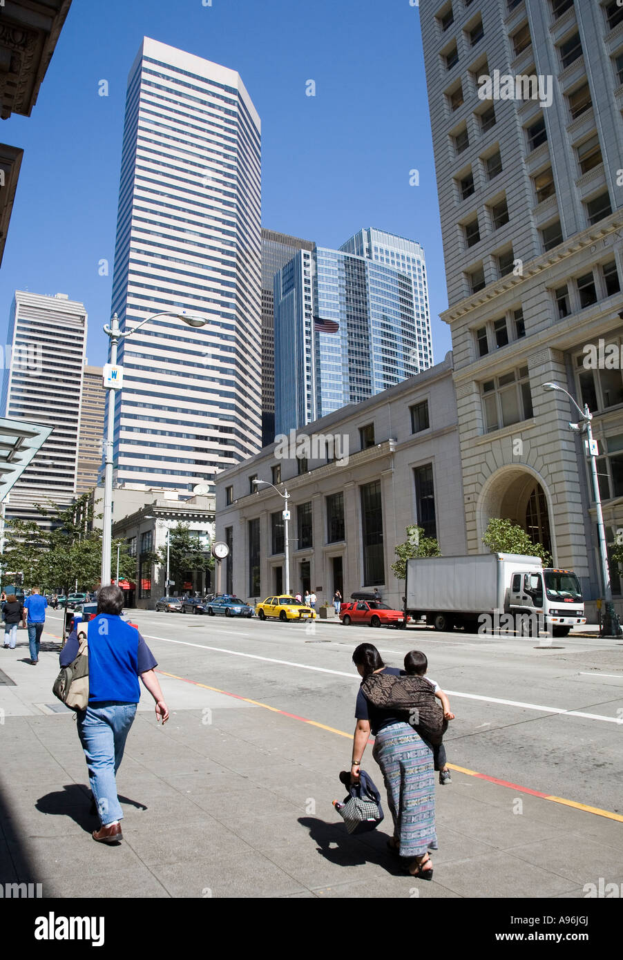 Woman carrying child on hip laden with bag walking through downtown ...
