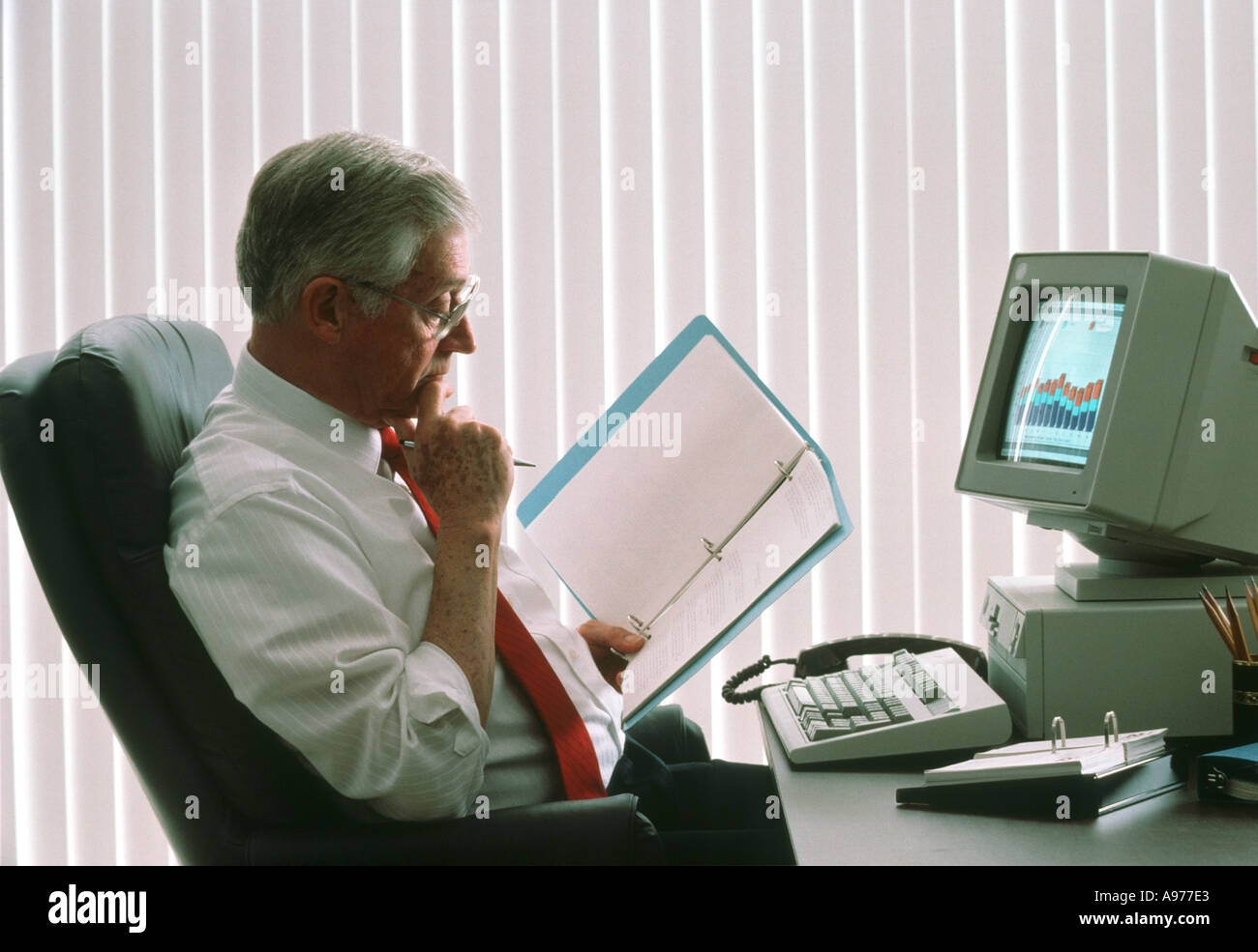 male business executive reading a computer report at his desk Stock ...