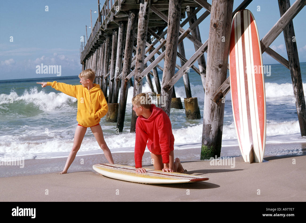 two boys under a pier at the beach waxing surfboards Stock Photo - Alamy