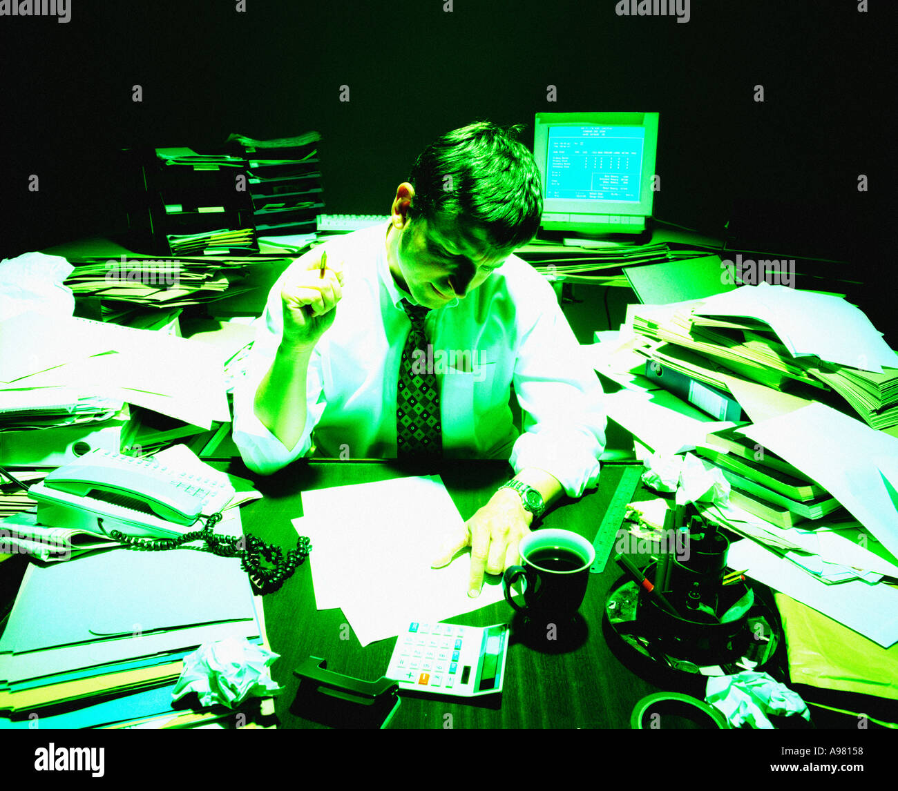 STRESSED BUSINESS EXECUTIVE AT DESK SURROUNDED BY PILES OF PAPERWORK ...