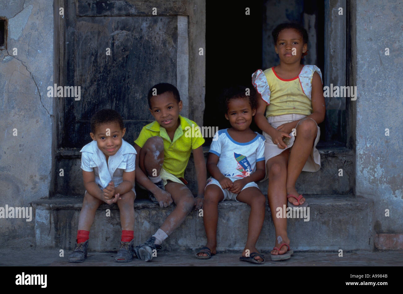 Four children sit on the front stoop of their home in a building on the ...