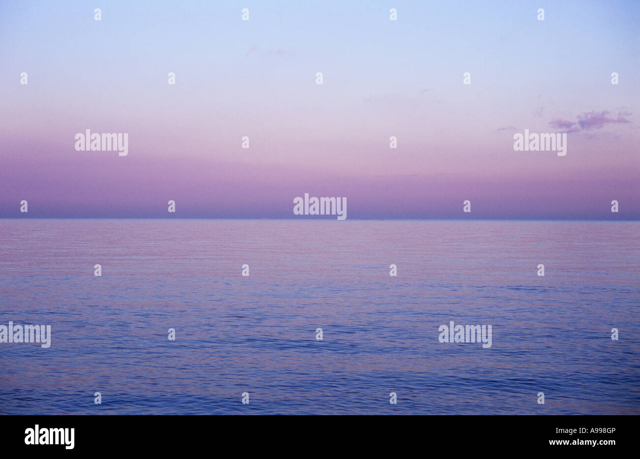 Flat calm silver sea tinged with pink of clear dawn or sunset sky with ...