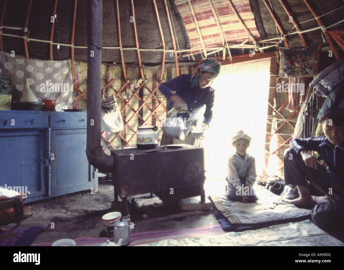 Kyrgyz mother and sons inside tent, yurta. She's pouring water for tea ...