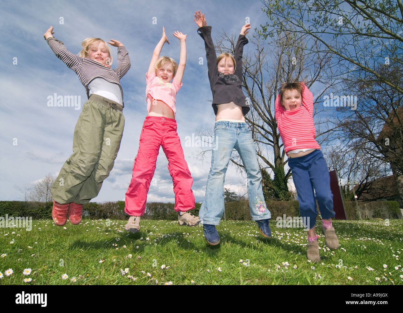 Four young girls 7 and 8 years old jumping on grass with daisy Stock ...