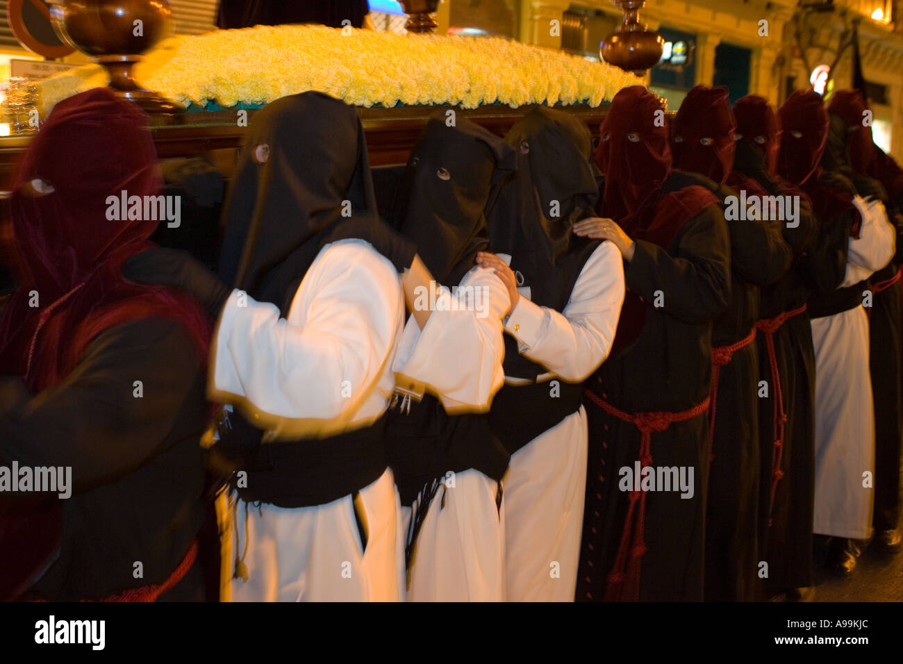 Hooded members of a religious fraternity wearing robes carry a float ...