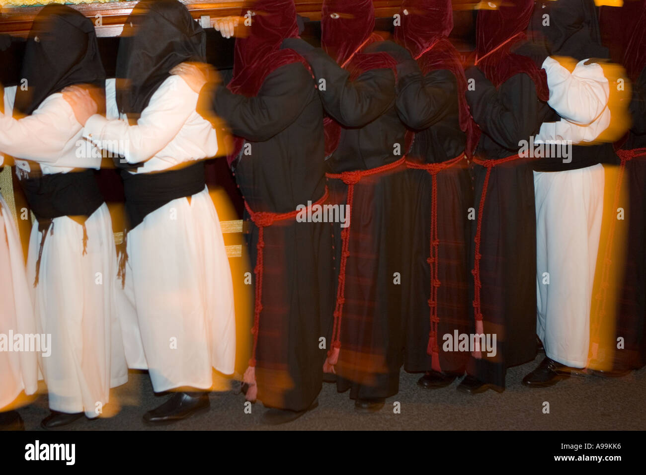 Hooded members of a religious fraternity wearing robes carry a float ...
