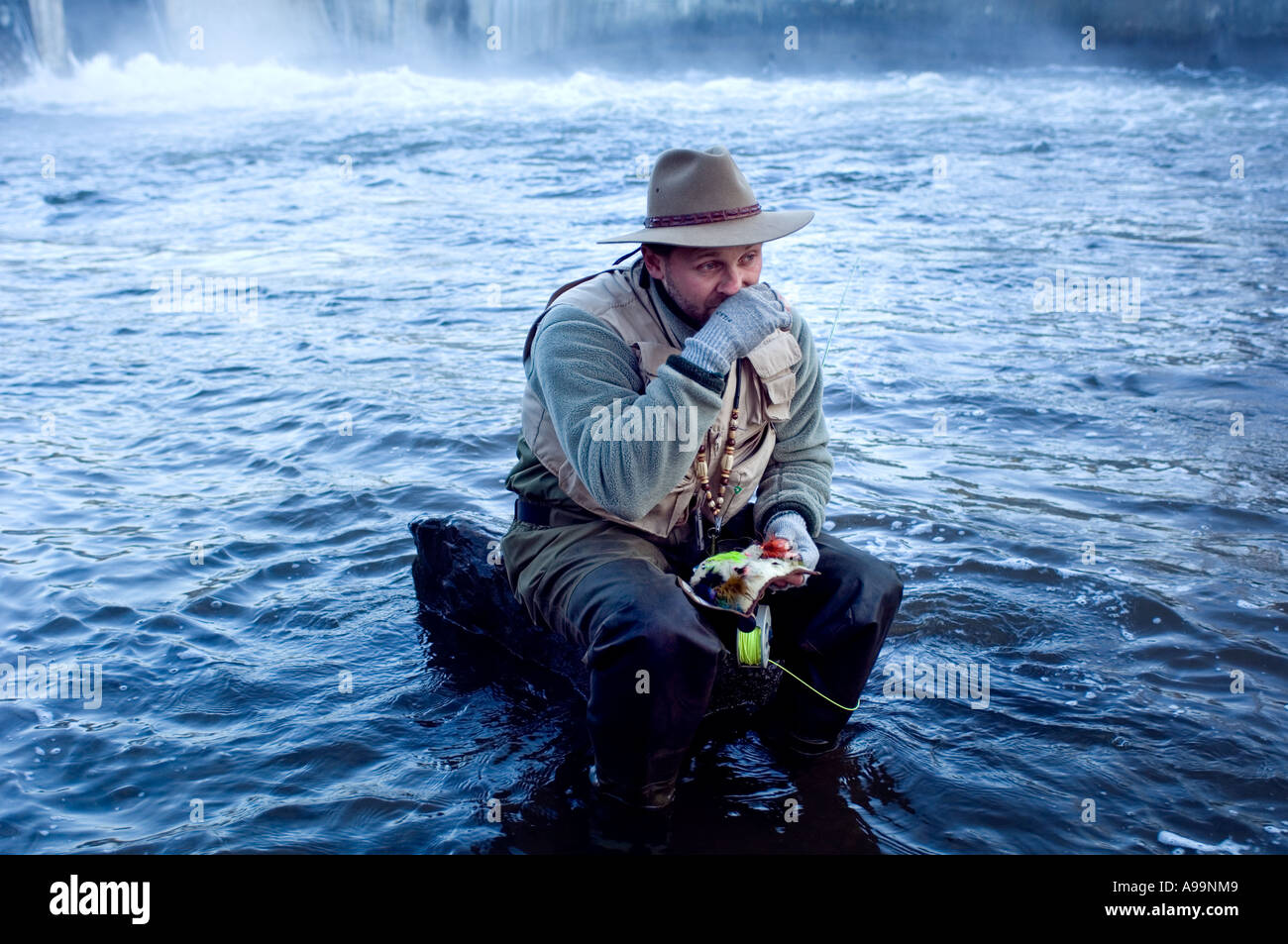 Man sitting on a rock in a river while taking a break from fly fishing ...