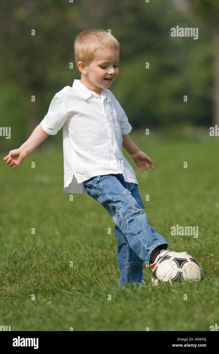 A young blonde boy playing football in the park on a sunny spring day ...