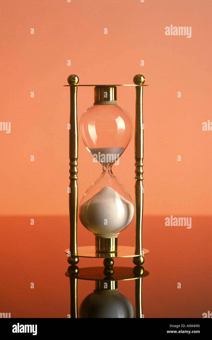 SAND FALLING THROUGH BRASS HOURGLASS SAND TIMER ON ORANGE BACKGROUND ...