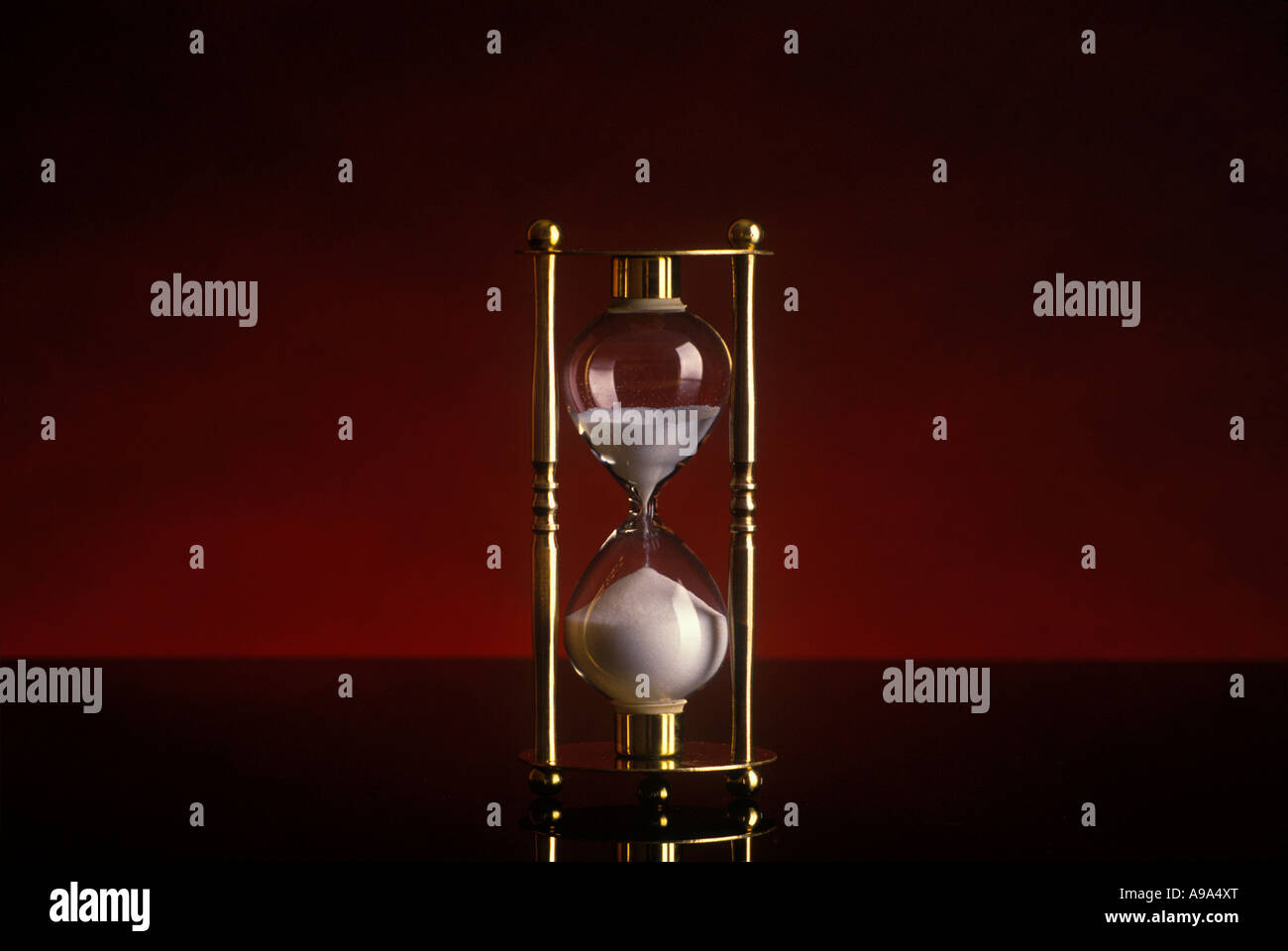 SAND FALLING THROUGH BRASS HOURGLASS SAND TIMER ON DARK RED BACKGROUND ...