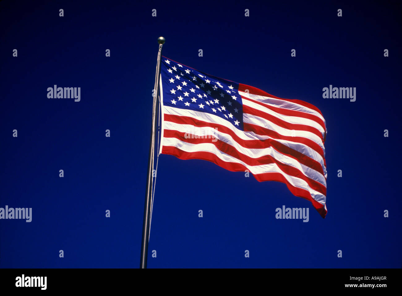 RIPPLING UNITED STATES FLAG FLYING ON FLAGPOLE WITH CLEAR BLUE SKY ...