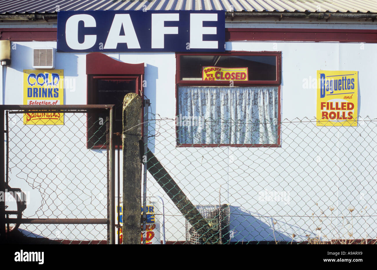 Detail of roadside cafe surrounded by wire link fence and with signs ...