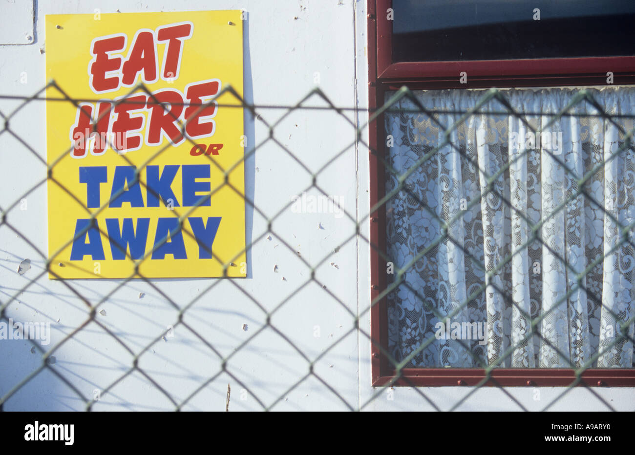 Sign on the side of a roadside cafe surrounded by wire link fence ...