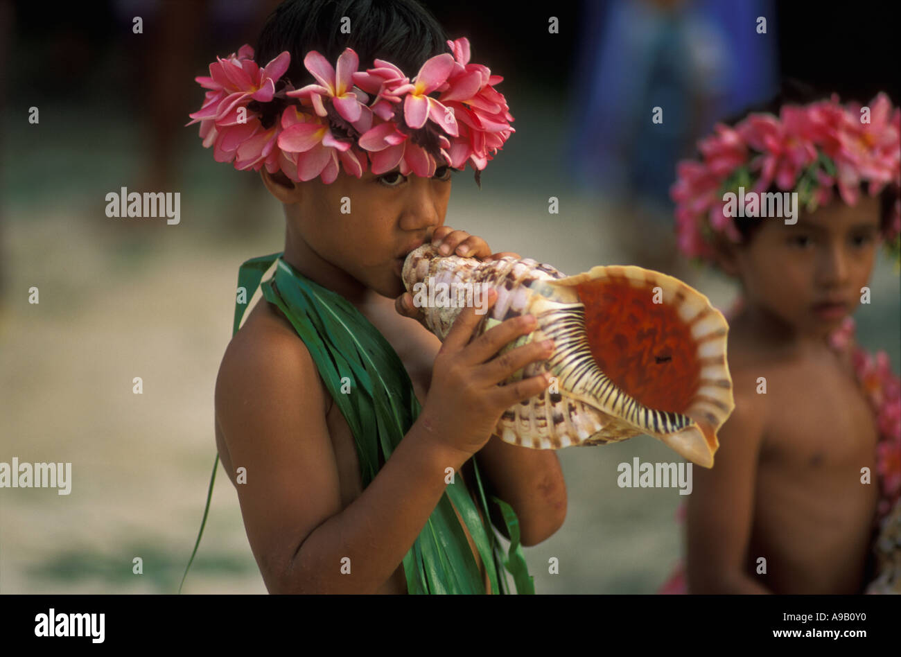A boy with a flower wreath on his head blows a conch shell at the 6th ...