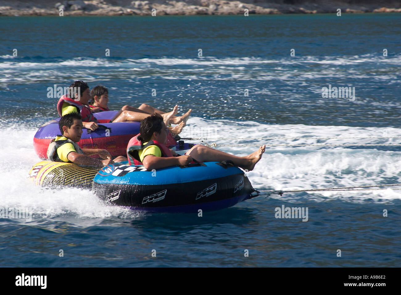Four teenagers being pulled on inflatable donuts by speed boat Stock ...