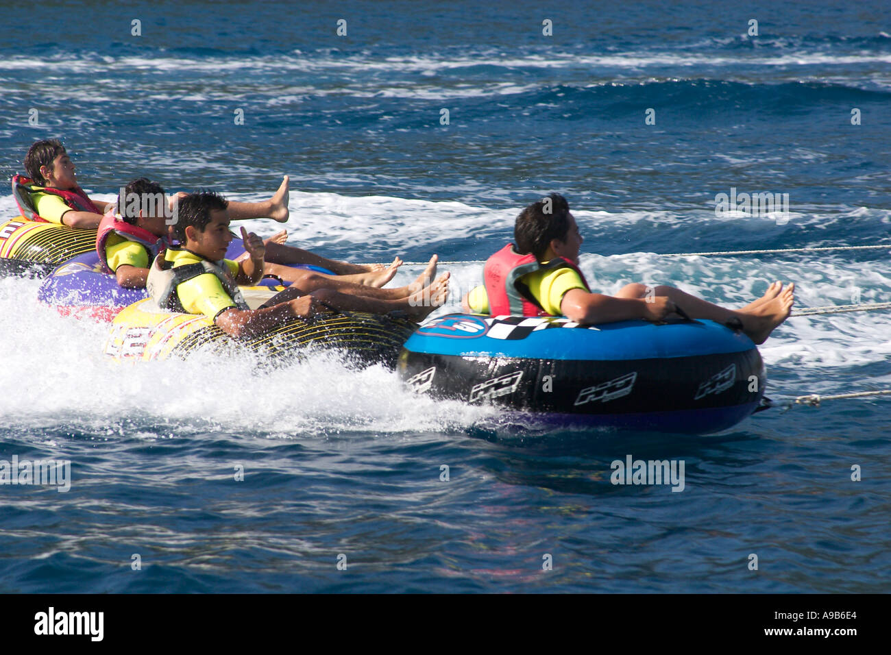 Four teenagers being pulled on inflatable donuts by speed boat Stock ...