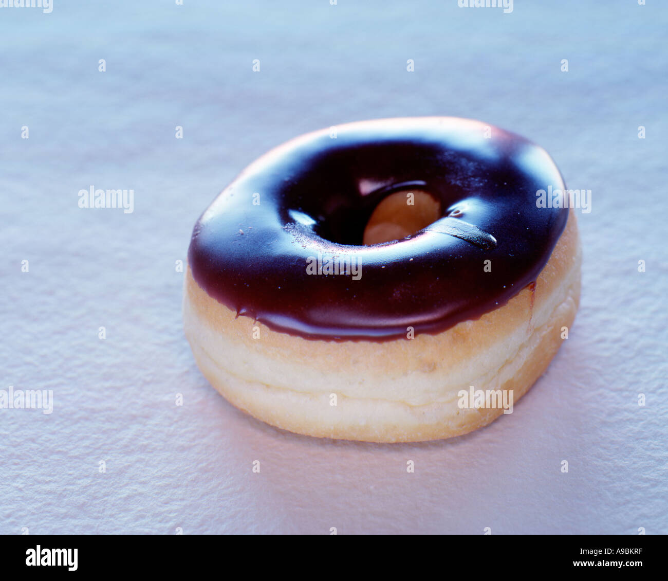 Donut glazed with dark chocolate icing on textured paper surface Stock ...