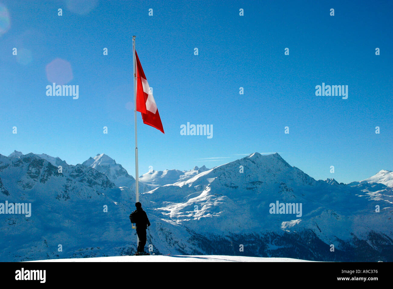 Skier standing below Swiss flag on the slopes at St Moritz Switzerland ...
