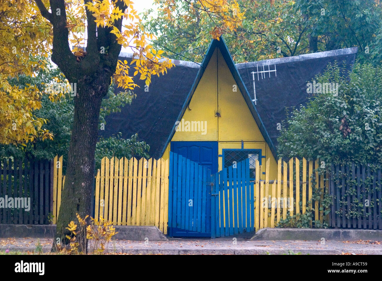Quaint Polish house in yellow and blue with tall picket fence. Highway ...