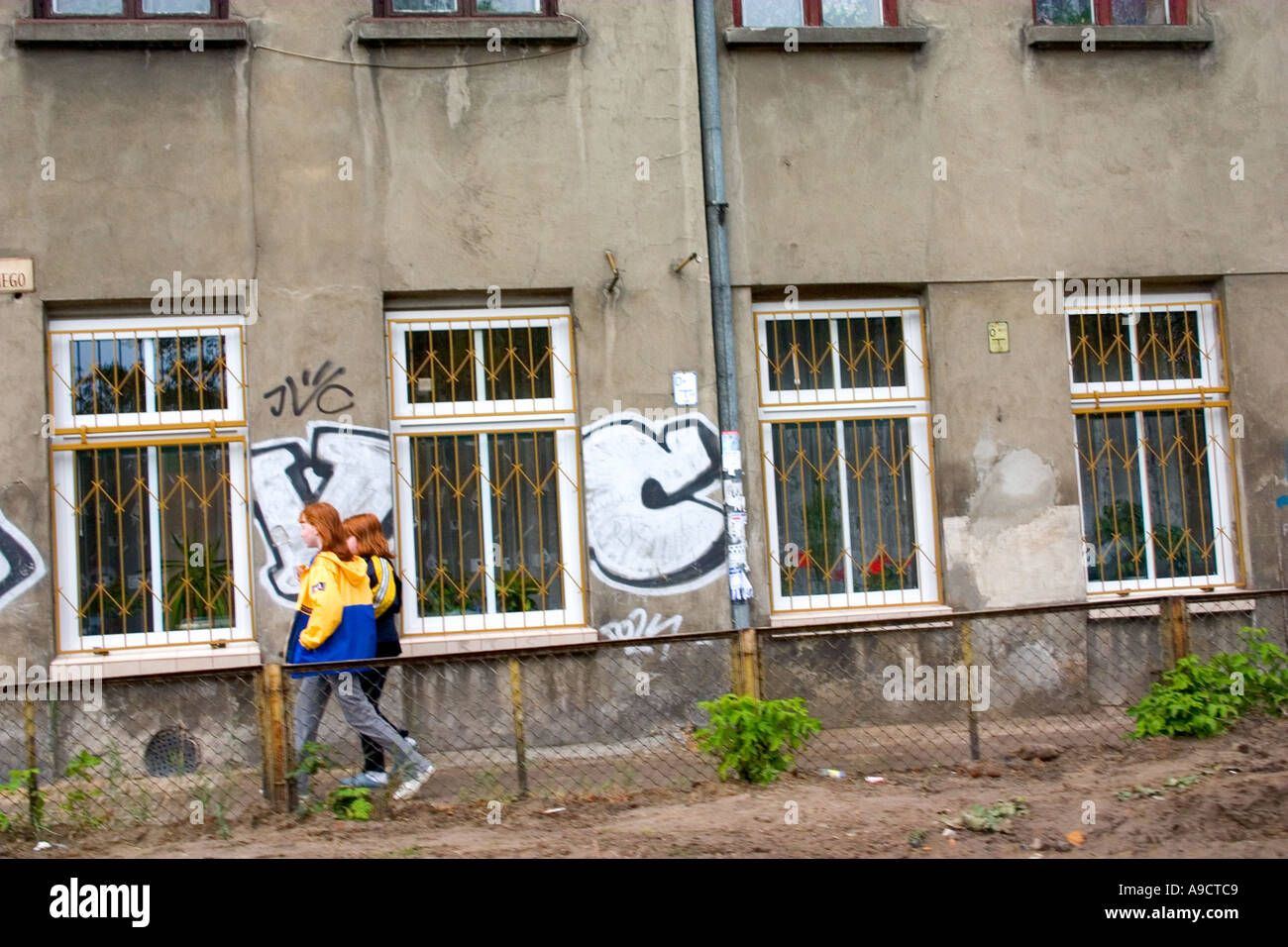 Two girls with red hair walking beside a graffiti lined building with ...