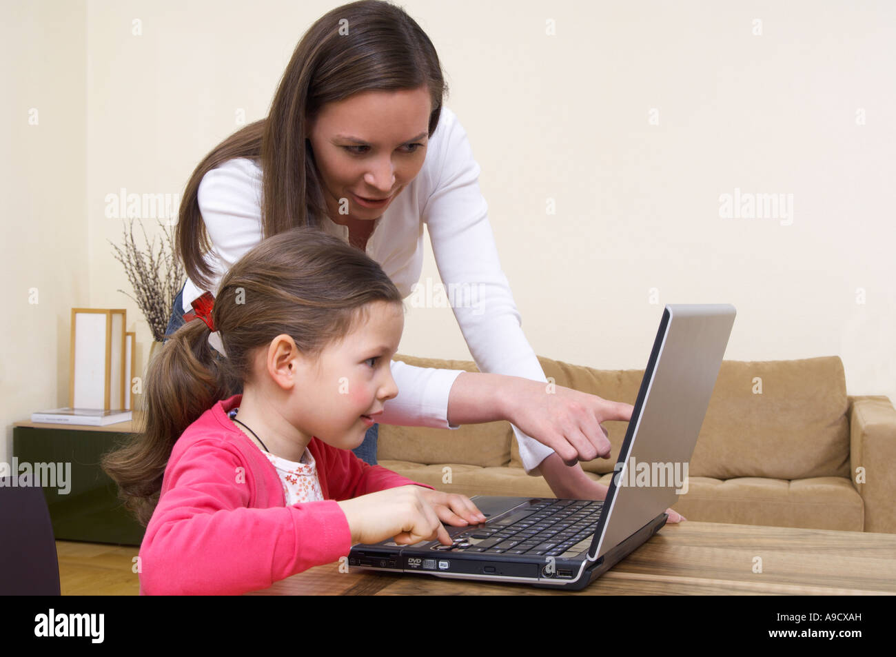 young mother showing little daughter how to work with laptop computer ...
