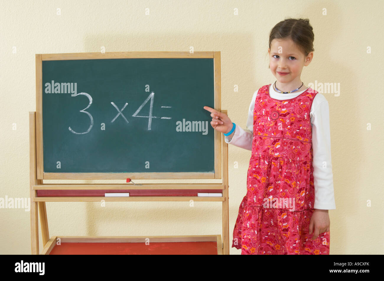 portrait of little girl pointing at blackboard with calculating problem ...