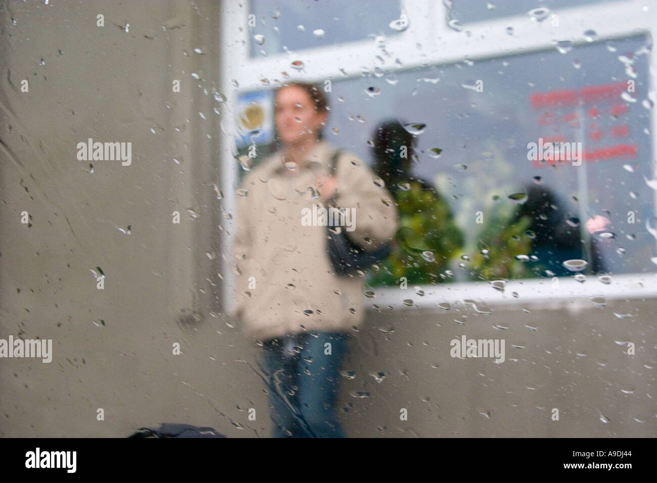 Woman waiting outside at grocery store with rain on car window ...