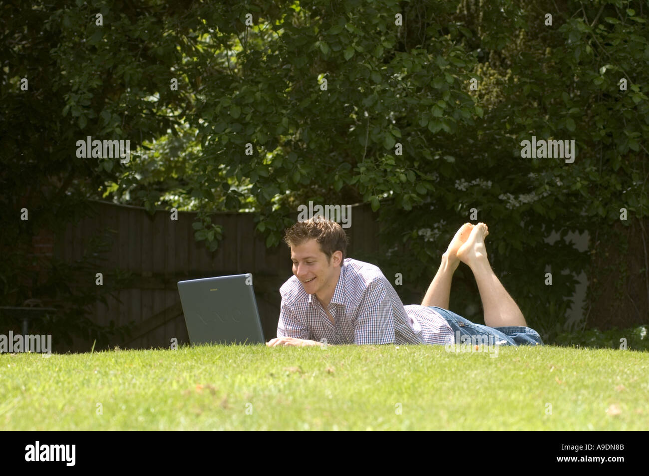 Young man on a laptop computer in a park or garden with grass in ...