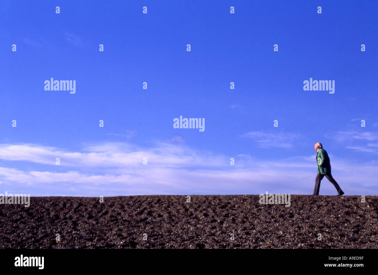 Lone man strutting across shingle beach Stock Photo - Alamy