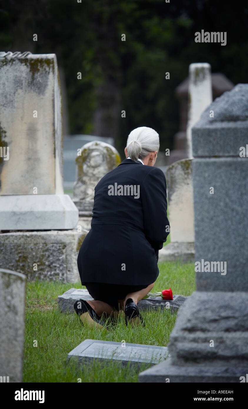 A senior woman places a rose on a gravestone in a cemetary Stock Photo ...