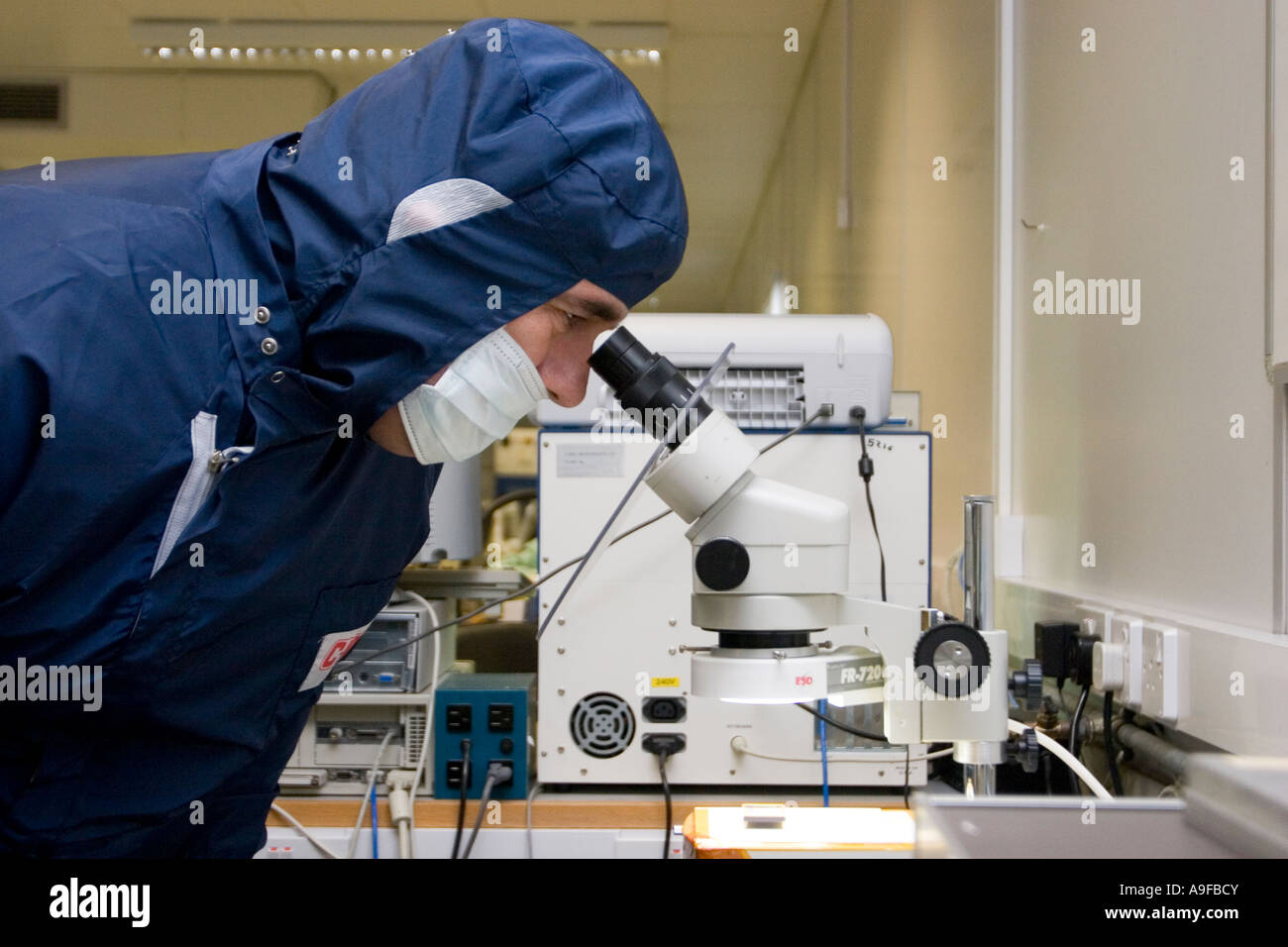 Man in clean room suit peers through microscope at CMAC Micro ...