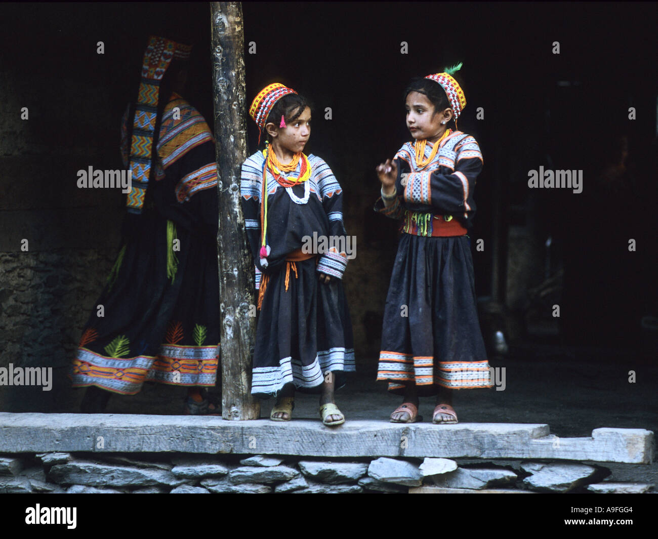 two local Kalash girls in traditional clothes with woman in background ...