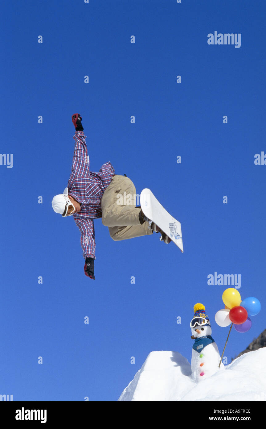 snowboader jumping in midair, with blue sky and snowman in background ...