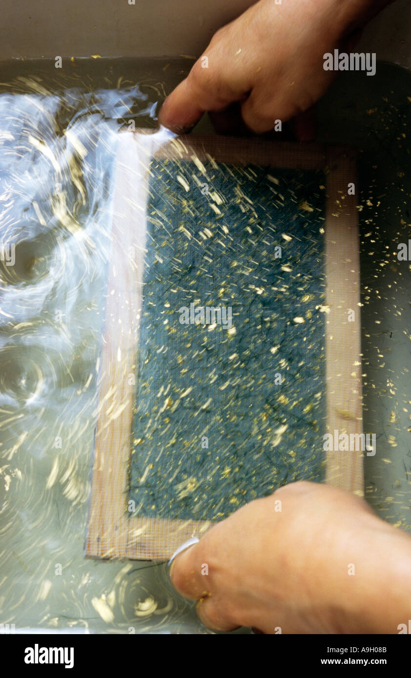 Handmade paper scooping a sheet of green paper with gold leaf out of a ...