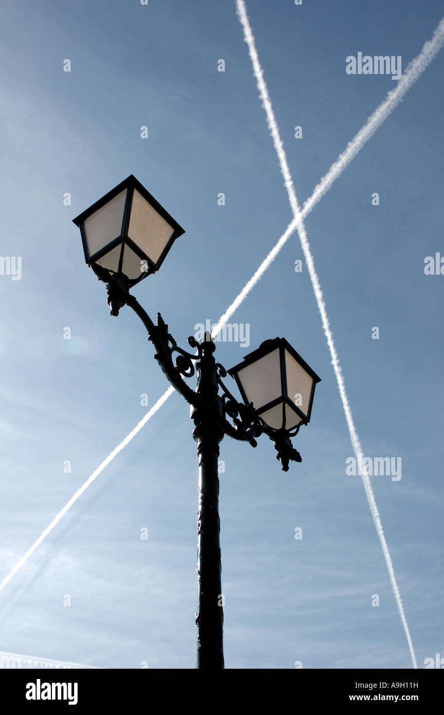 Aircraft jet trails cross high above traditional lamp post in ...