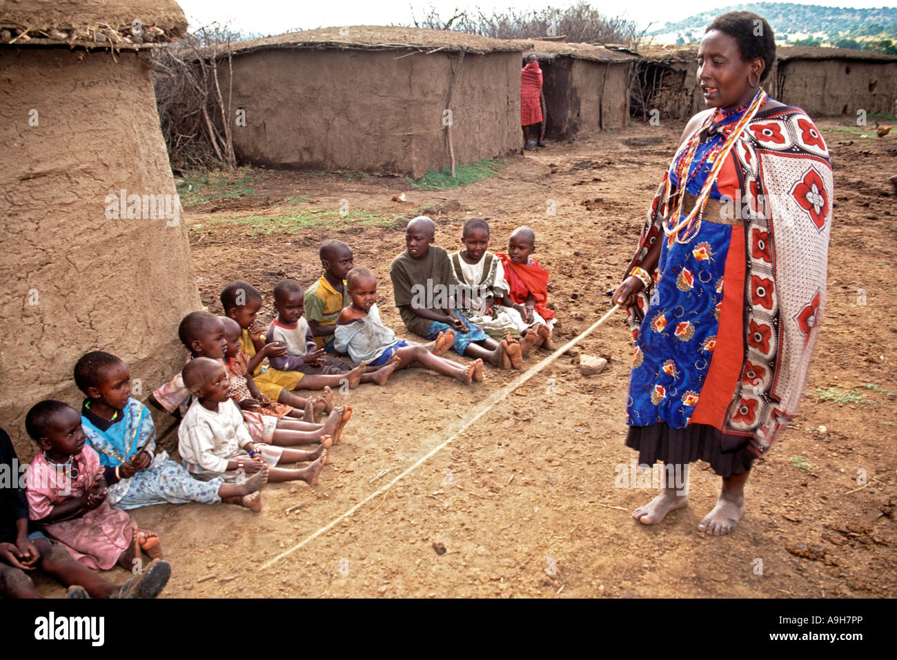 A Masai lady teaching a group of children in their village (called a ...