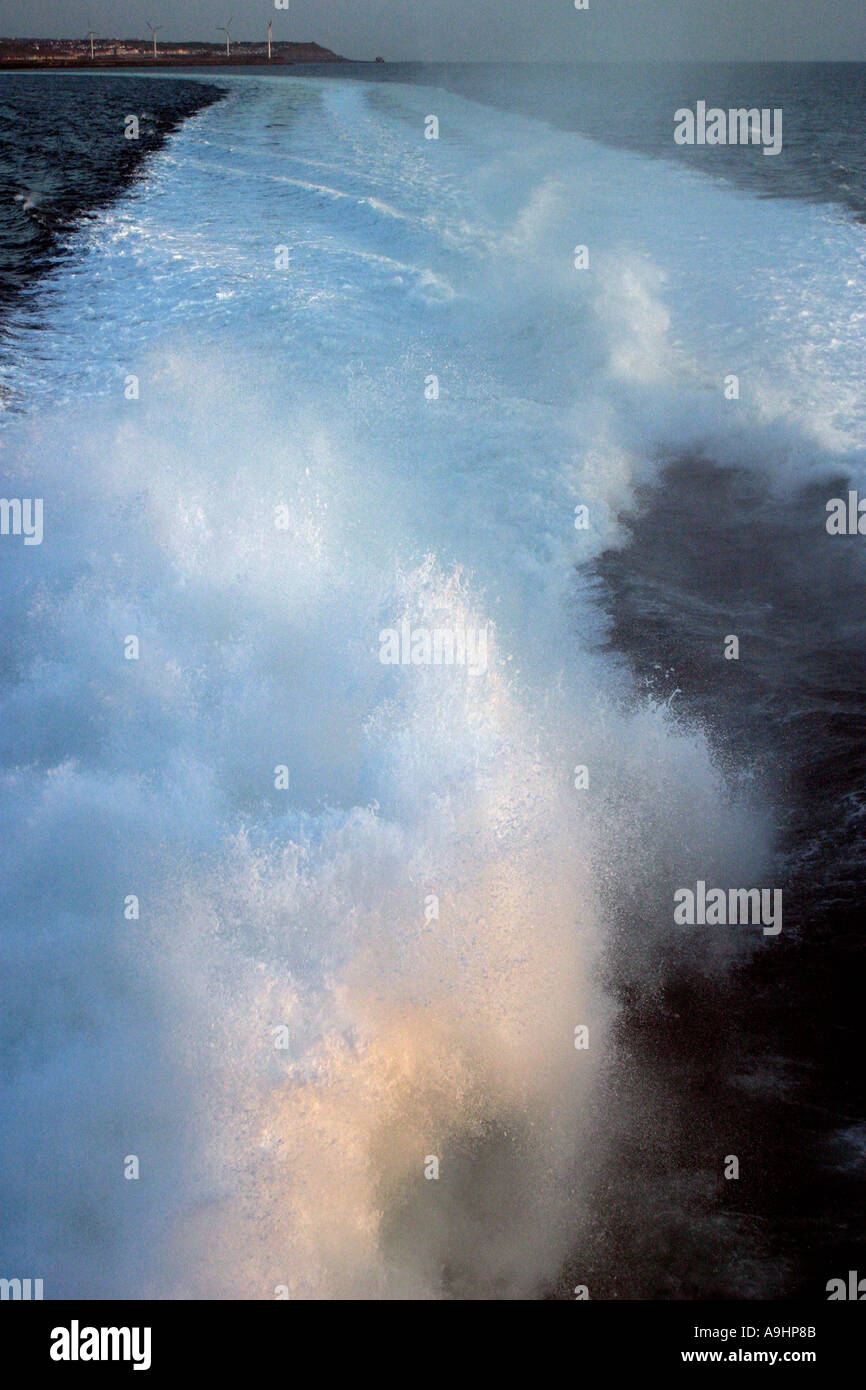 Wake from stern of cross channel catamaran catches the low evening sun ...