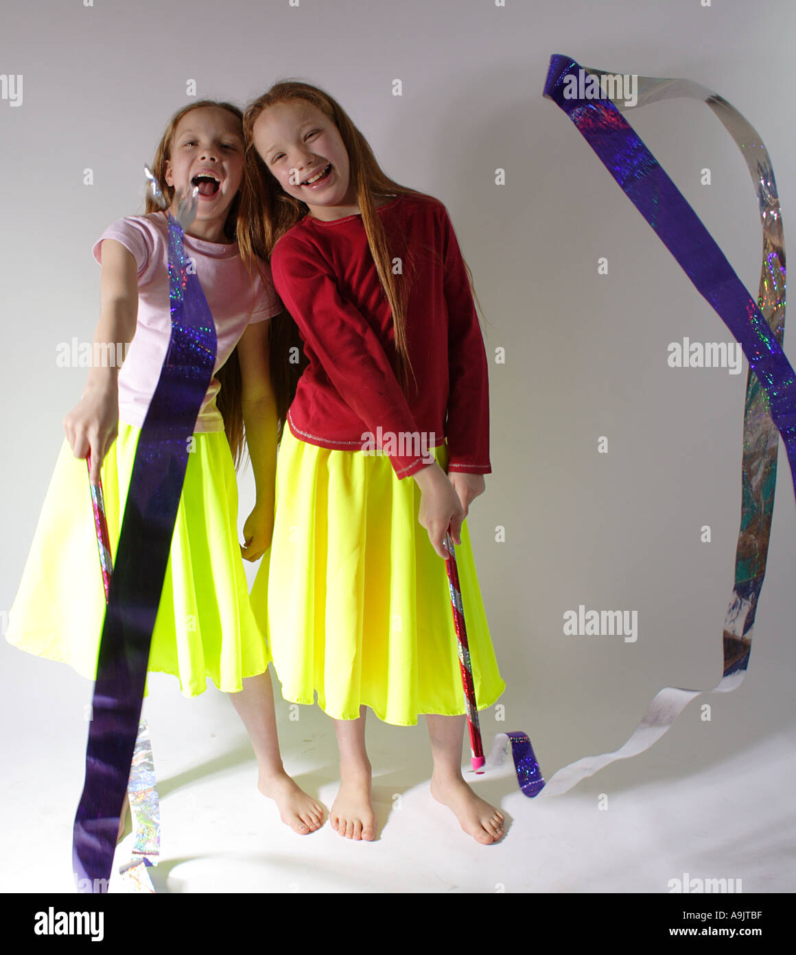 Twin sisters in colourful outfits playing with ribbons Stock Photo - Alamy